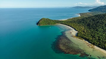 Vista aérea de uma área costeira com praia, águas cristalinas e uma península arborizada.