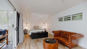 Quarto com cama, sofá de couro, mesa redonda pequena e janela com persianas.