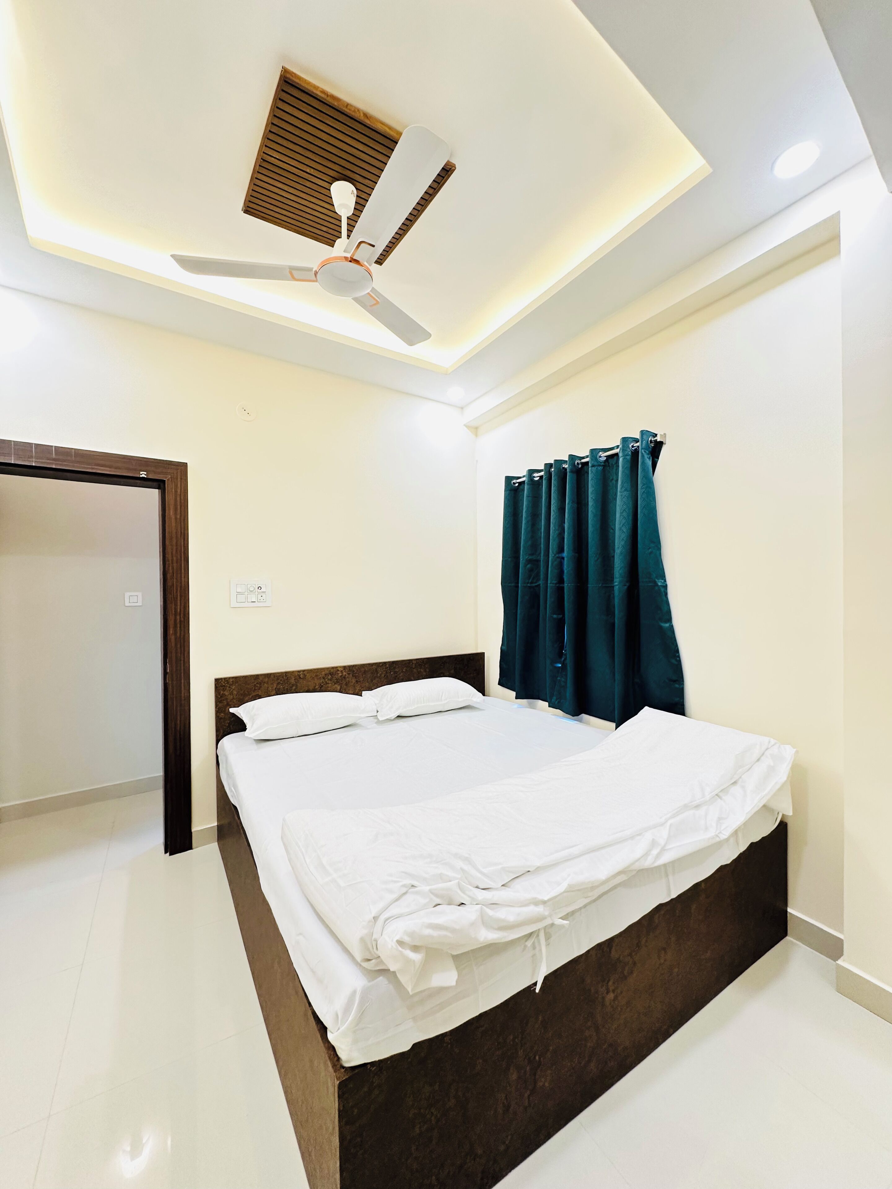 Quarto com cama, ventilador de teto e janela com cortinas.