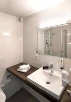 Casa de banho moderna com lavatório branco, espelho e área de chuveiro.