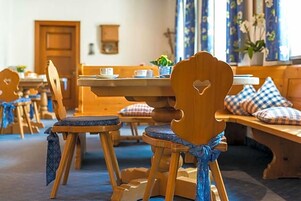 Uma área de refeições acolhedora com mobiliário de madeira, incluindo cadeiras e um banco, e uma mesa com xícara e pires.