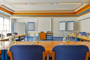 Uma sala de conferências com mesas, cadeiras e telas de projeção.