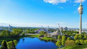 Um parque com um lago, uma torre e edifícios modernos.