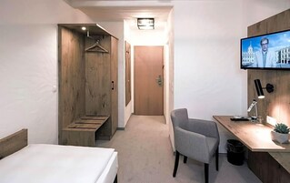Quarto de hotel com cama, escrivaninha com computador, cadeira, televisão fixada na parede e armário de madeira.