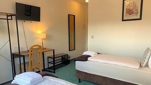 Quarto de hotel com duas camas, uma escrivaninha, uma cadeira, televisão e obras de arte na parede.