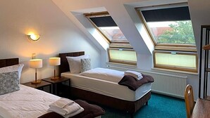 Quarto de hotel com duas camas, uma janela, um radiador e uma mesa de cabeceira com luminárias.