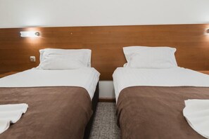 Quarto duplo com cama de casal, cabeceira de madeira e duas almofadas brancas.