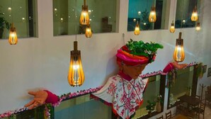 Uma área de refeições com várias mesas e cadeiras, um arranjo decorativo de plantas e luminárias pendentes.