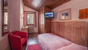 Quarto com uma cama de casal, uma cadeira vermelha, televisão e janela com cortinas.