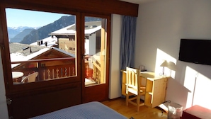 Quarto com cama, escrivaninha, cadeira, televisão e vista para uma montanha.