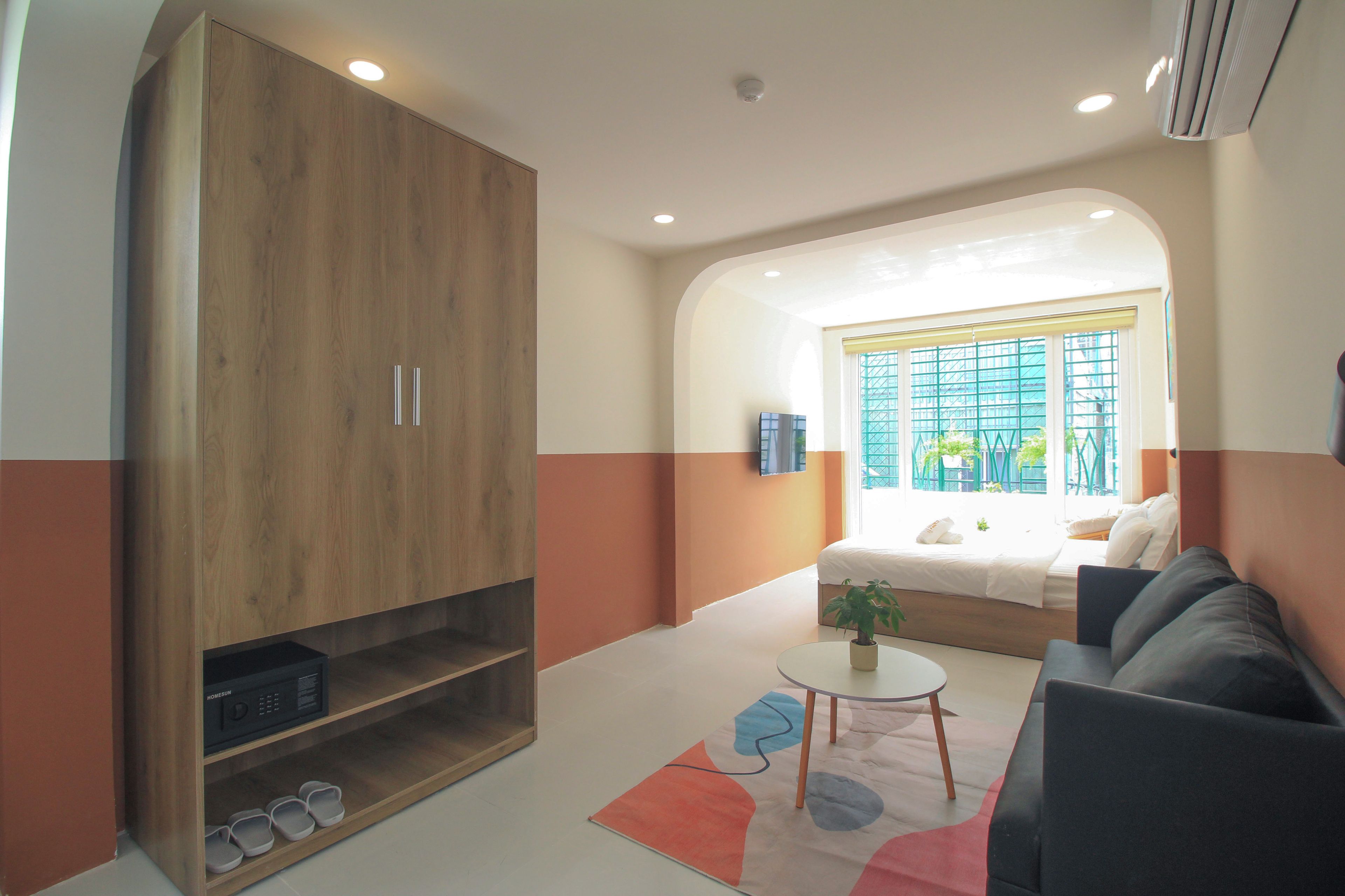Quarto de hotel moderno com um guarda-roupa espaçoso, um sofá, uma mesa pequena e uma cama com vista para o verde lá fora.