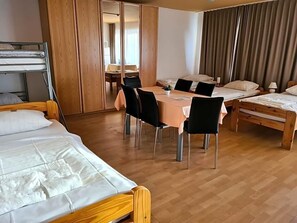 Quarto de hotel com uma cama beliche, uma mesa de jantar com cadeiras e uma cama separada.