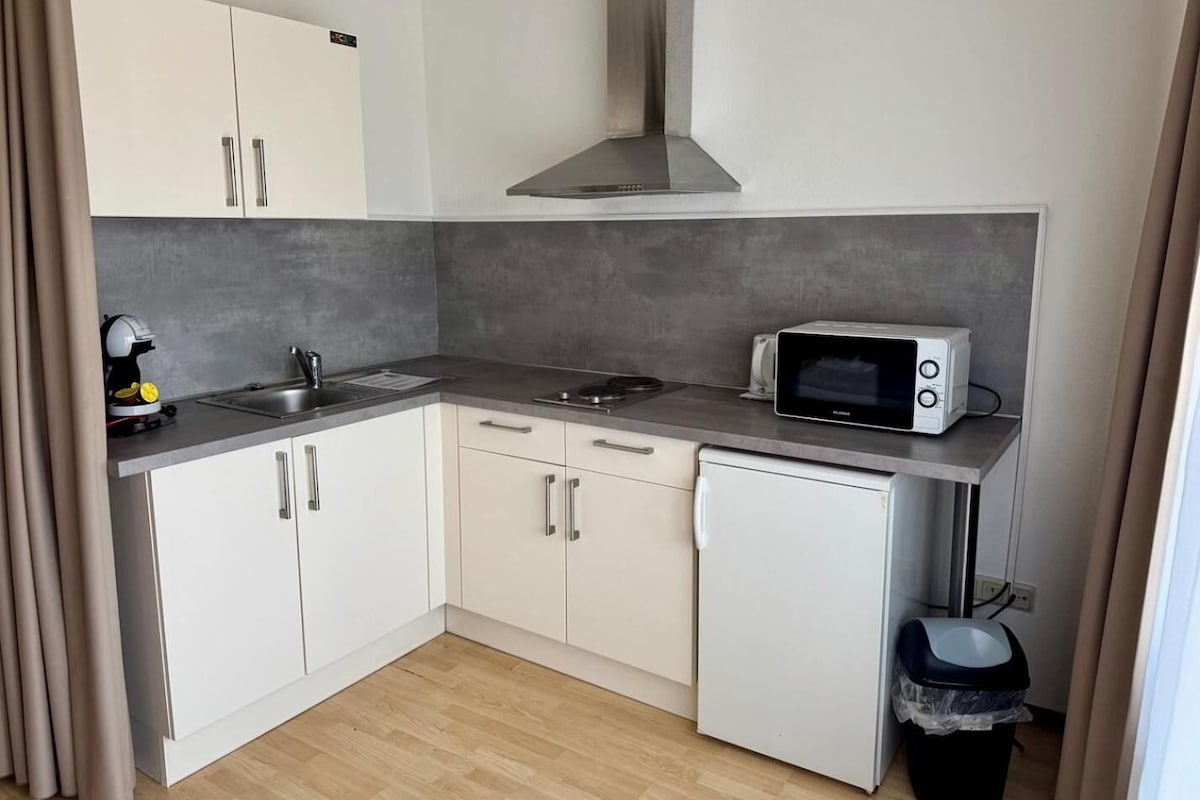 Cozinha compacta com armários brancos, coifa em aço inoxidável, micro-ondas e lixeira.