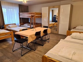 Quarto de hotel com beliches, uma mesa de jantar com cadeiras, um espelho e um guarda-roupa.