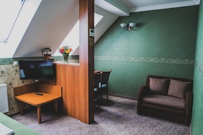 Quarto com televisão, secretária de madeira, cadeira e sofá.