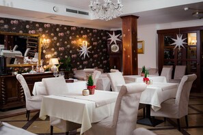 Uma sala de jantar com mesas preparadas para quatro pessoas, um lustre e papel de parede floral.