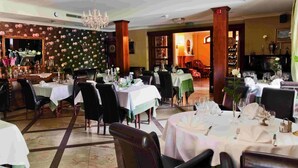 Restaurante com várias mesas preparadas para refeições, um candelabro e um design floral na parede.