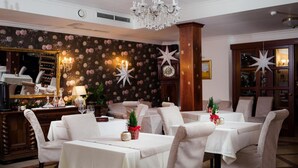 Uma sala de jantar com mesas preparadas para quatro pessoas, um lustre e papel de parede floral.
