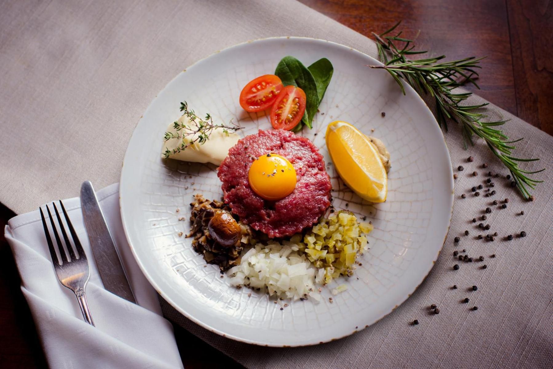 Um prato com carne crua, um ovo cozido e alguns vegetais.