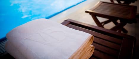 Área de piscina com uma toalha em uma cadeira e um banco de madeira.