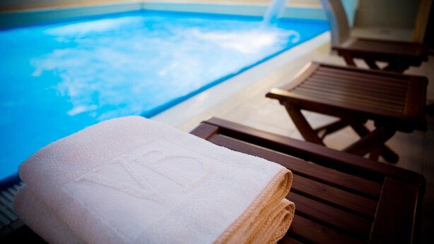 Área de piscina com uma toalha em uma cadeira e um banco de madeira.