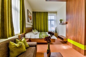 Quarto de hotel com uma cama, um sofá, uma mesinha de madeira, um vaso com flores e um quadro na parede.