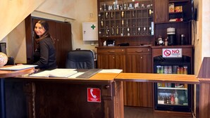 Bancada de recepção com placa de 'Proibido Fumar', um relógio e um aviso de 'Chamar Emergência'.
