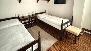 Quarto com duas camas de madeira, um banco, uma mesinha de cabeceira com luminárias e uma TV de tela plana na parede.