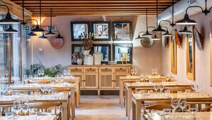 Interior de restaurante com várias mesas, cadeiras e luminárias pendentes.