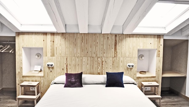 Quarto moderno com cabeceira de madeira, uma cama grande, duas mesas de cabeceira e um claraboia acima.