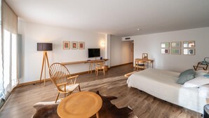 Quarto de hotel com cama, escrivaninha, cadeira, televisão e obras de arte nas paredes.