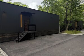 Um edifício moderno com fachada escura, um deck de madeira e uma escadaria que leva a uma entrada.