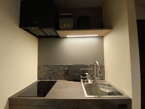 Cozinha com design moderno, destacando uma pia de aço inoxidável, painel de fundo preto e forno embutido.