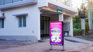 Um edifício com uma placa de identificação anunciando Auro Residency, exibindo números de contato e imagens de quartos e piscinas.