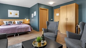 Quarto moderno com cama, duas poltronas, uma mesinha de centro com garrafa e copos, e um guarda-roupa.