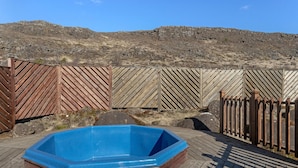 Uma banheira de hidromassagem em um deck de madeira, com uma paisagem montanhosa ao fundo.