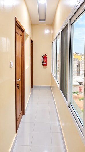 Corredor com extintor preso na parede, porta com fechadura e janela com vista para o exterior.