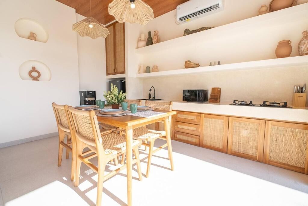 Cozinha moderna com armários de madeira, mesa de jantar com cadeiras e iluminação pendente.