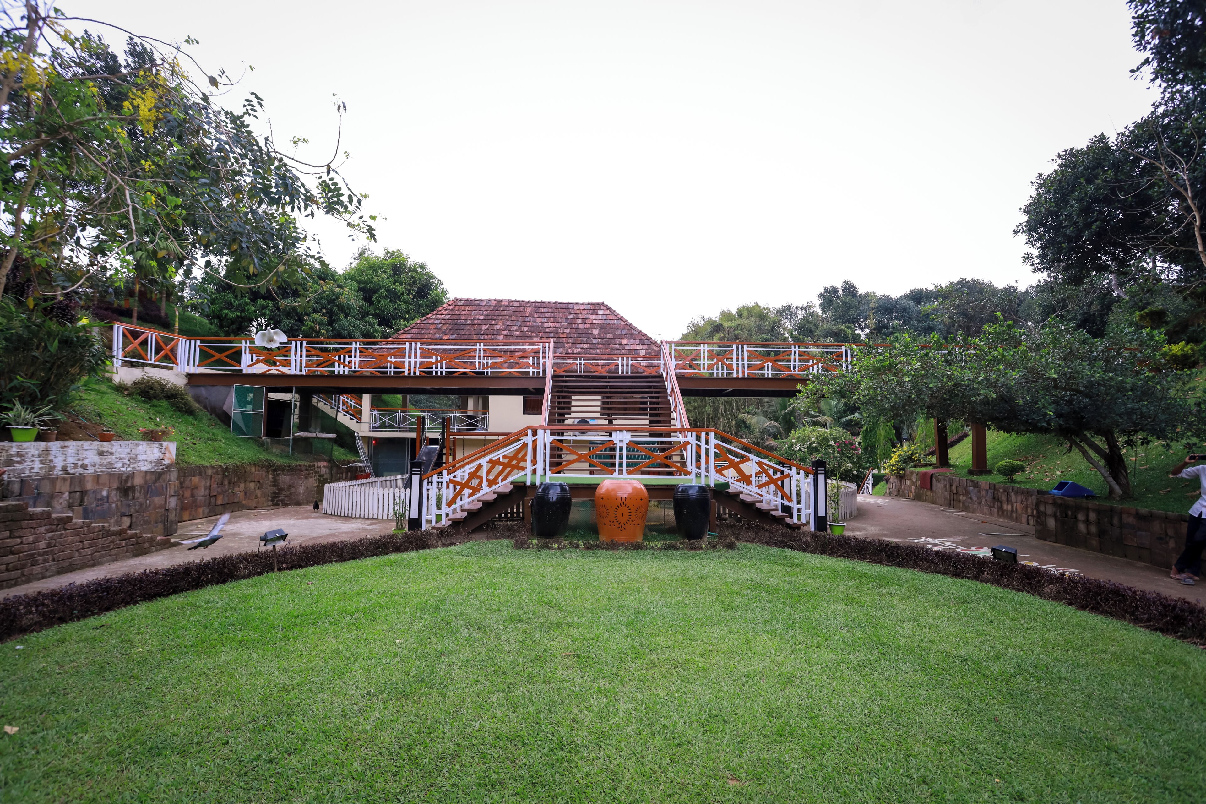 Edifício com escadaria que dá para uma varanda, cercado por um gramado bem cuidado e árvores.