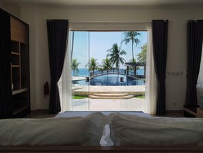 Quarto de hotel com uma cama grande, vista para piscina, palmeiras e uma ponte.