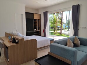 Quarto de hotel moderno com cama, escrivaninha, sofá e vista para palmeiras e uma piscina.