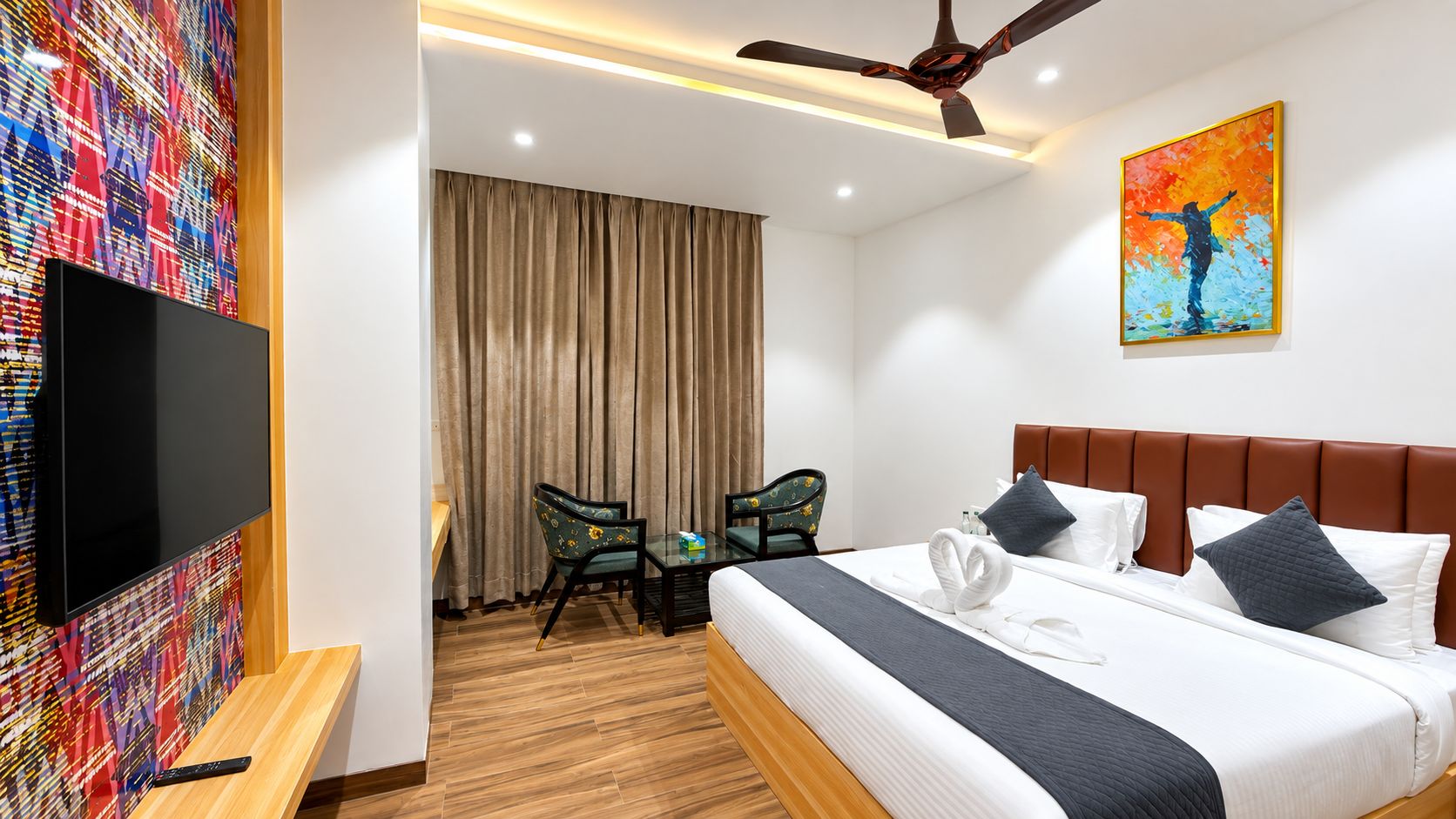 Quarto de hotel com cama, televisão, quadro e ventilador de teto.