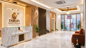 Uma área de recepção de hotel com um balcão de mármore, o logotipo de Daksh Hotels & Resorts e um design de interiores moderno.