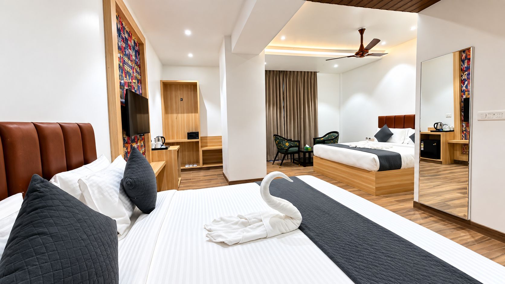 Quarto de hotel com uma cama grande, escrivaninha, cadeira, espelho e ventoinha no teto.