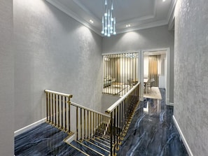 Uma escadaria com degraus de mármore e grades douradas, que leva a um quarto com vista.