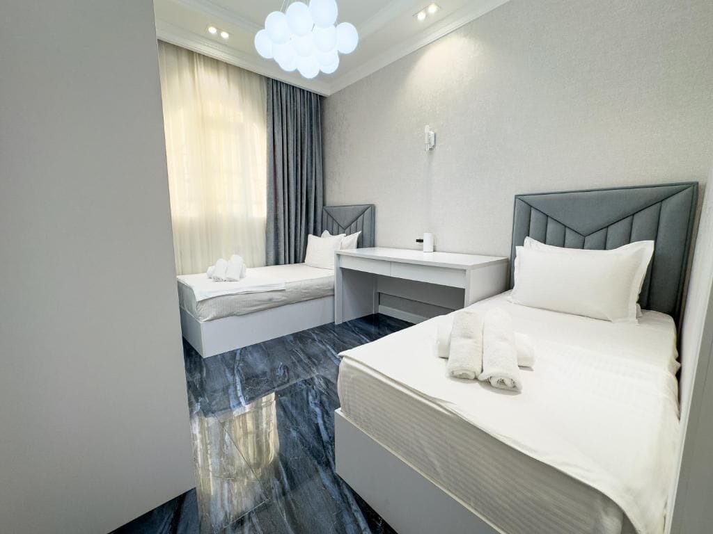 Quarto de hotel com duas camas, uma escrivaninha e uma janela grande com cortinas.