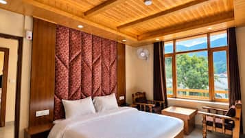 Um quarto espaçoso com uma cama grande, vigas de madeira no teto, uma janela com vista para o verde e um espaço de estar com mesa e cadeiras.