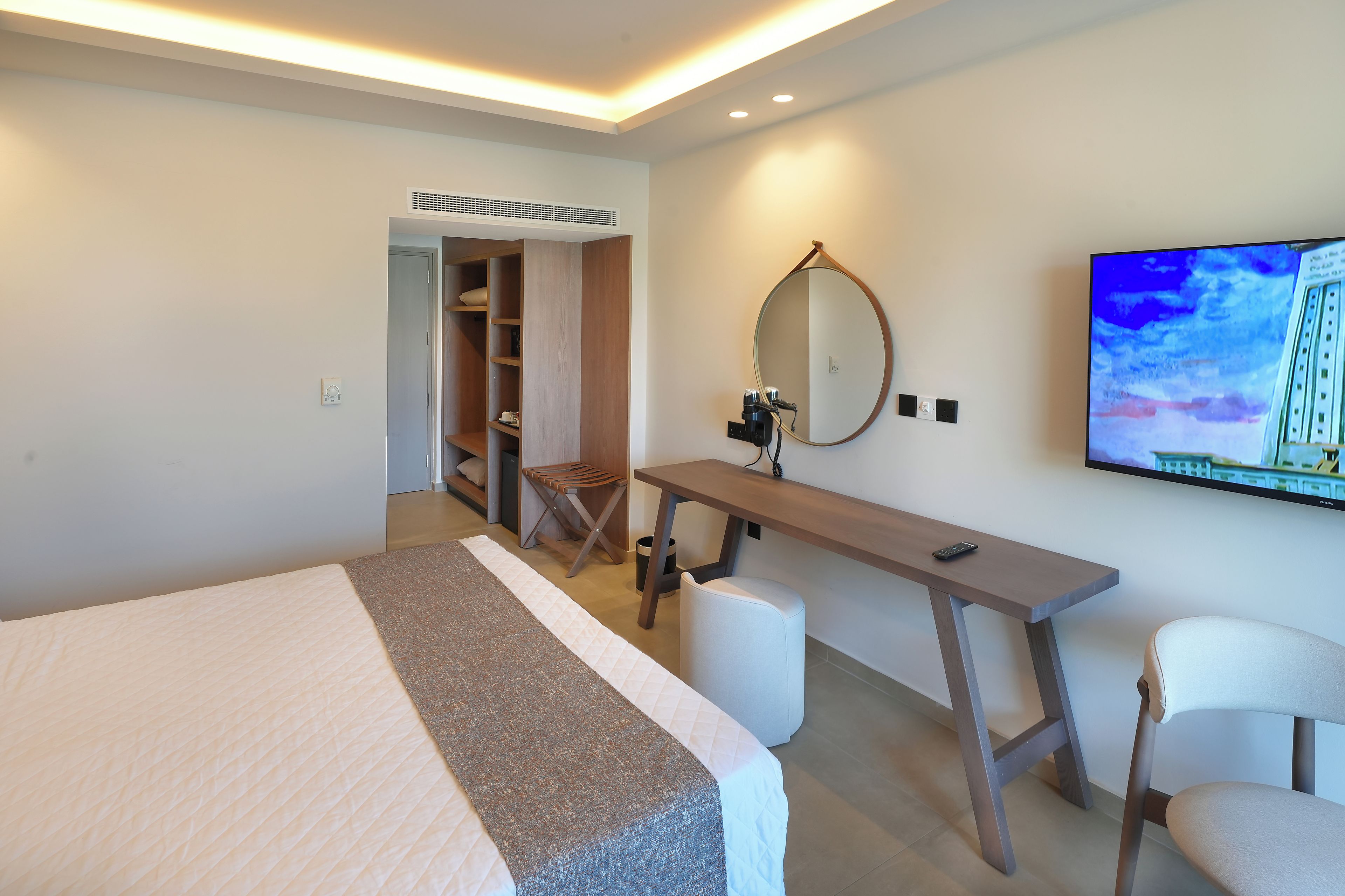 Quarto de hotel com cama, escrivaninha, cadeira, televisão e guarda-roupa.
