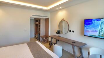 Quarto de hotel com cama, escrivaninha, cadeira, televisão e guarda-roupa.