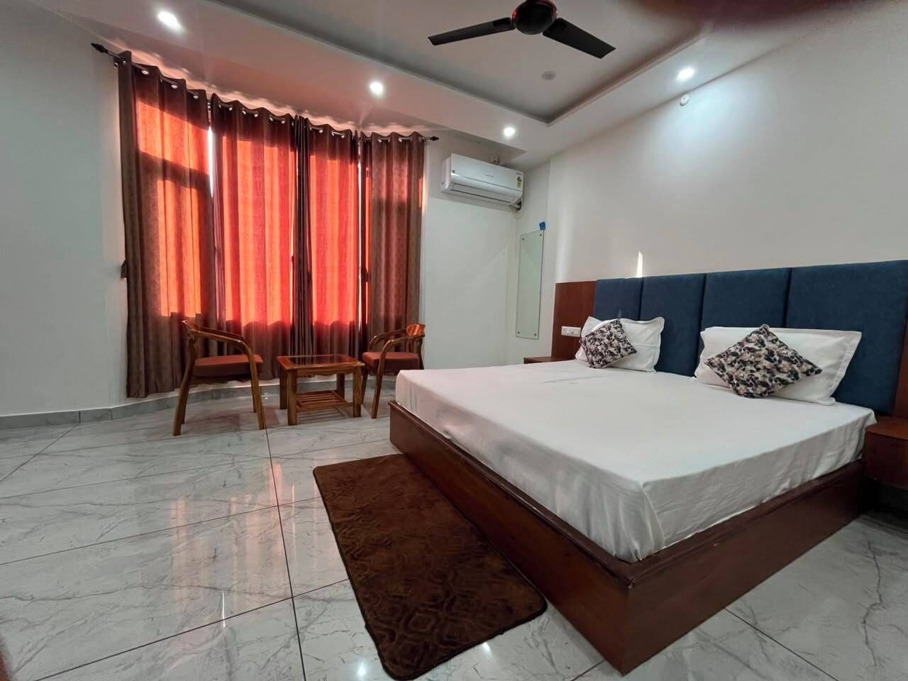 Quarto de hotel com cama, duas cadeiras, escrivaninha, ventilador de teto e ar condicionado.